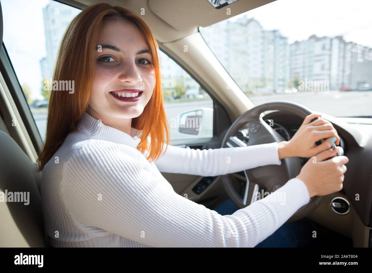 Young Redhead Woman Driver Behind A Wheel Driving A Car Smiling Happily