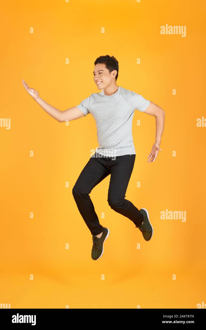 Energetic happy young Asian man in casual clothes jumping, studio shot ...