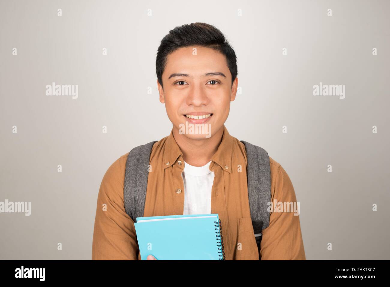 Portrait of smiling young college Asian student with books and backpack ...