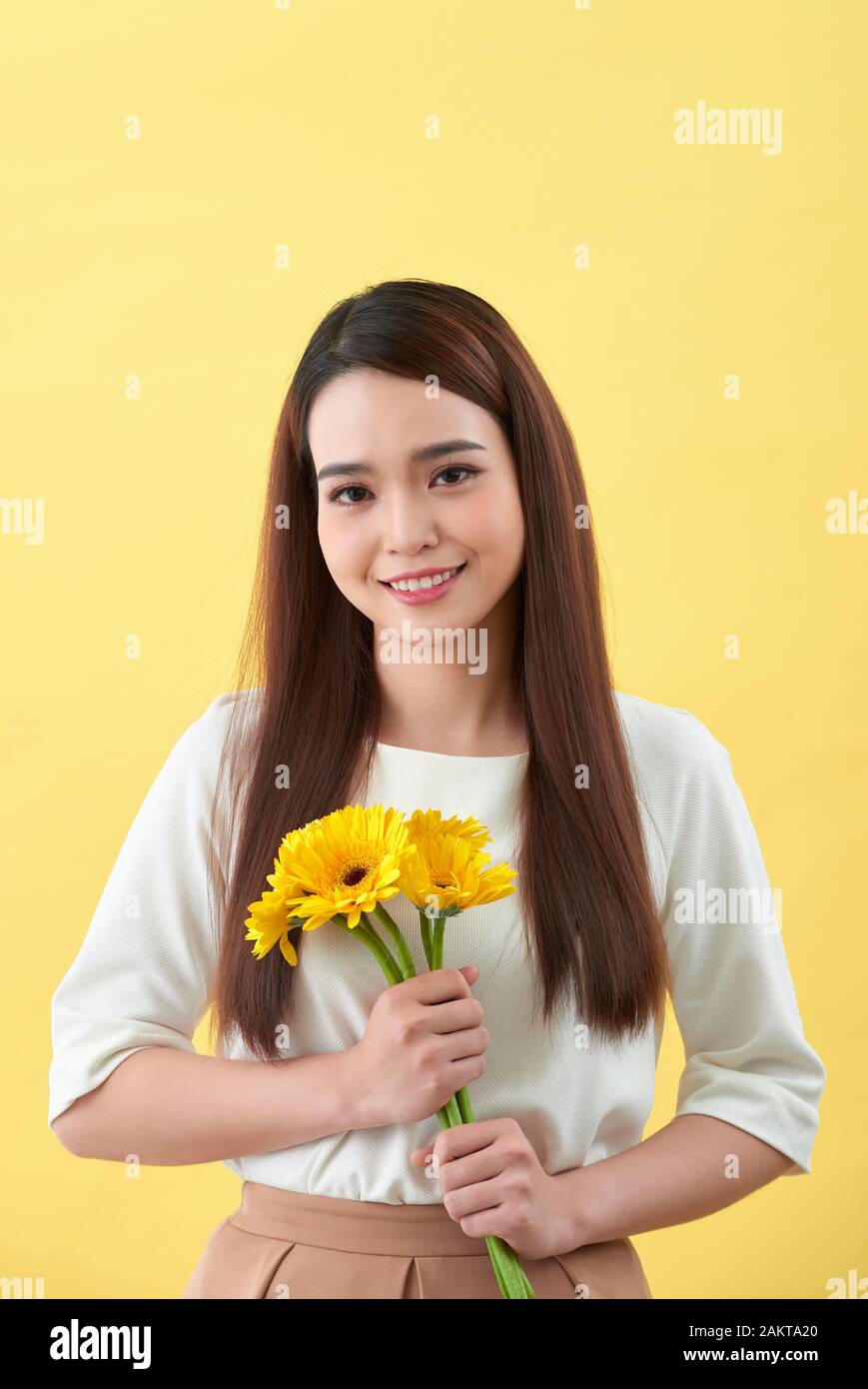 Happy young woman holding bouquet of flowers in her hand on yellow ...