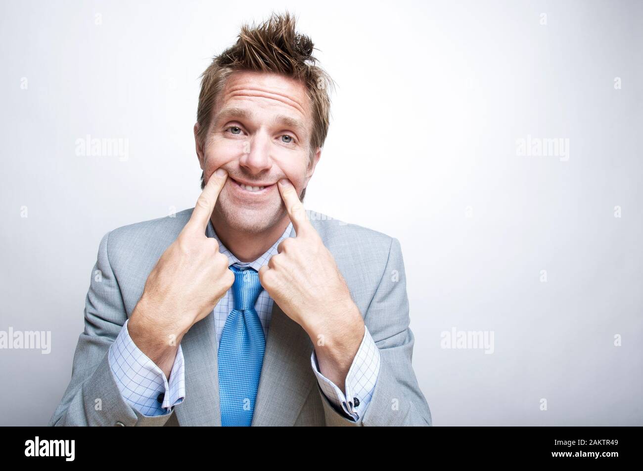 Tired businessman forcing a smile by holding up the corners of his ...