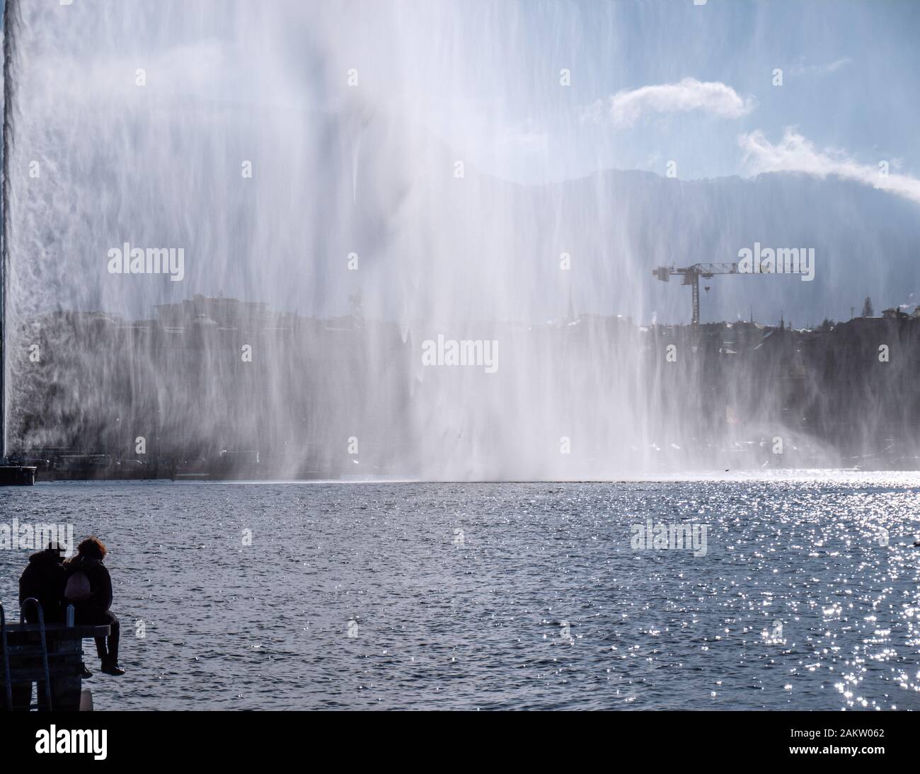 A couple watch the water spray from a large fountain from the a lake ...