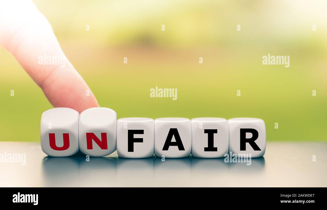Hand turns dice and changes the word unfair to fair Stock Photo - Alamy