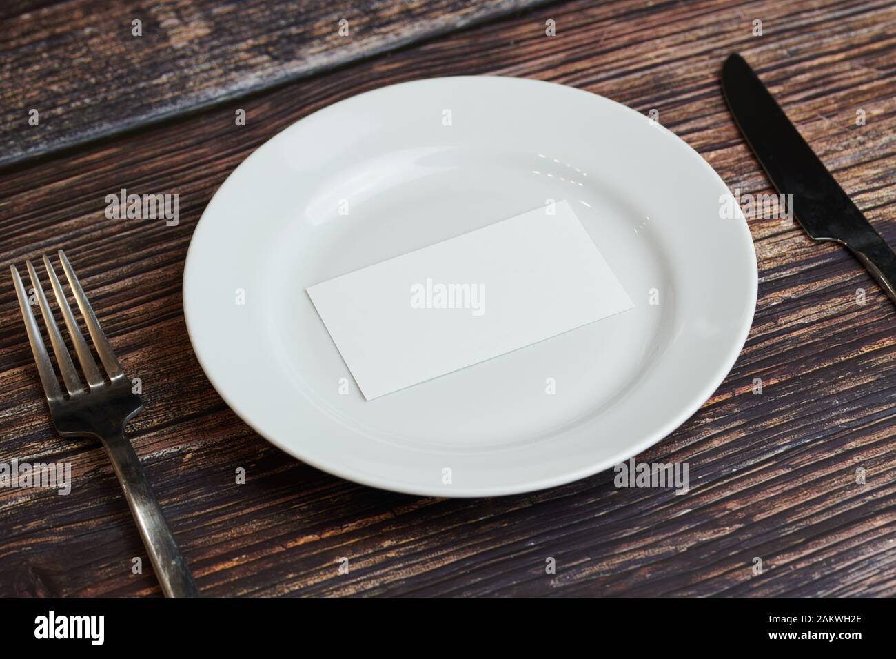 Empty plate on table with cutlery and blank business card, top view ...