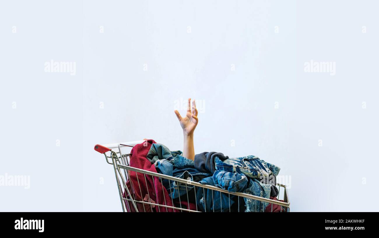 Female hand sticks out of shopping cart full of clothes. Shopaholism ...
