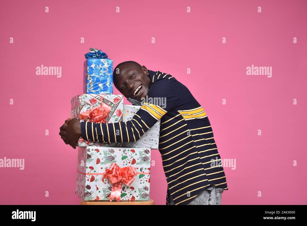 excited young black man feeling excited, hugging a stack of gift boxes ...