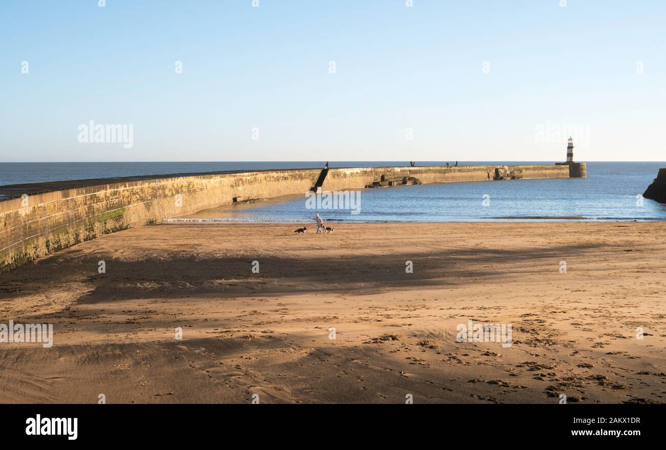 Woman walking dog on slope beach and anglers fishing off the north pier ...