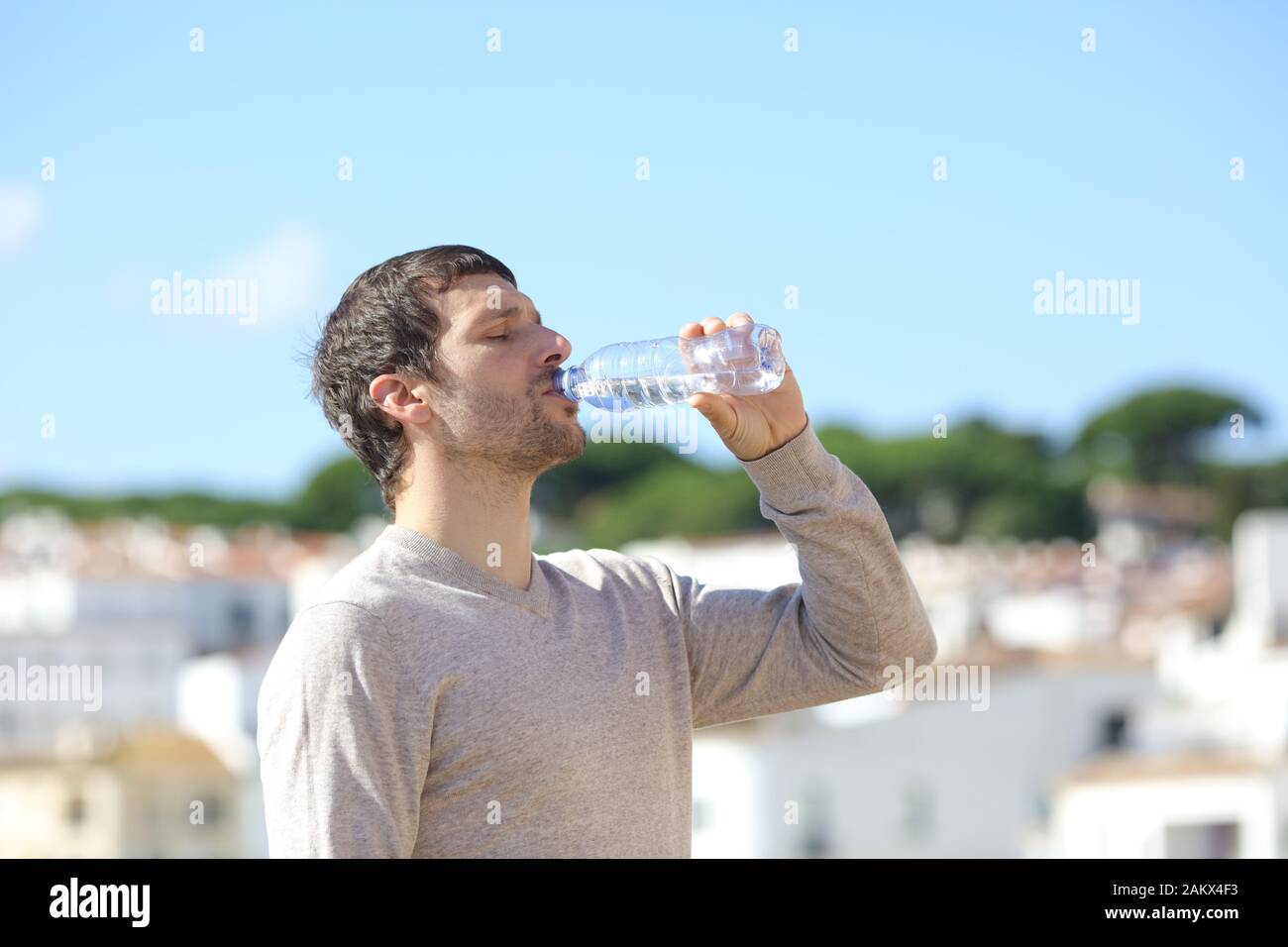 Profile of a casual adult man drinking bottled water standing in a town ...
