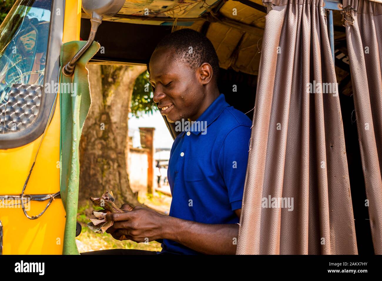 young african man driving a rickshaw taxi counting his money smiling ...