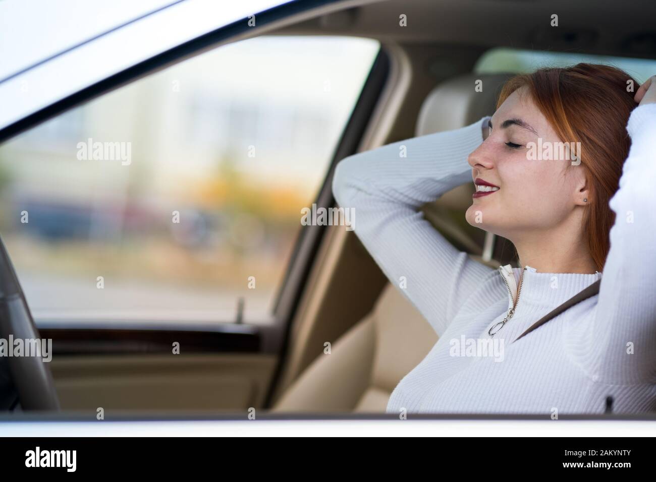 Young redhead woman driver fastened by seatbelt resting in a car ...