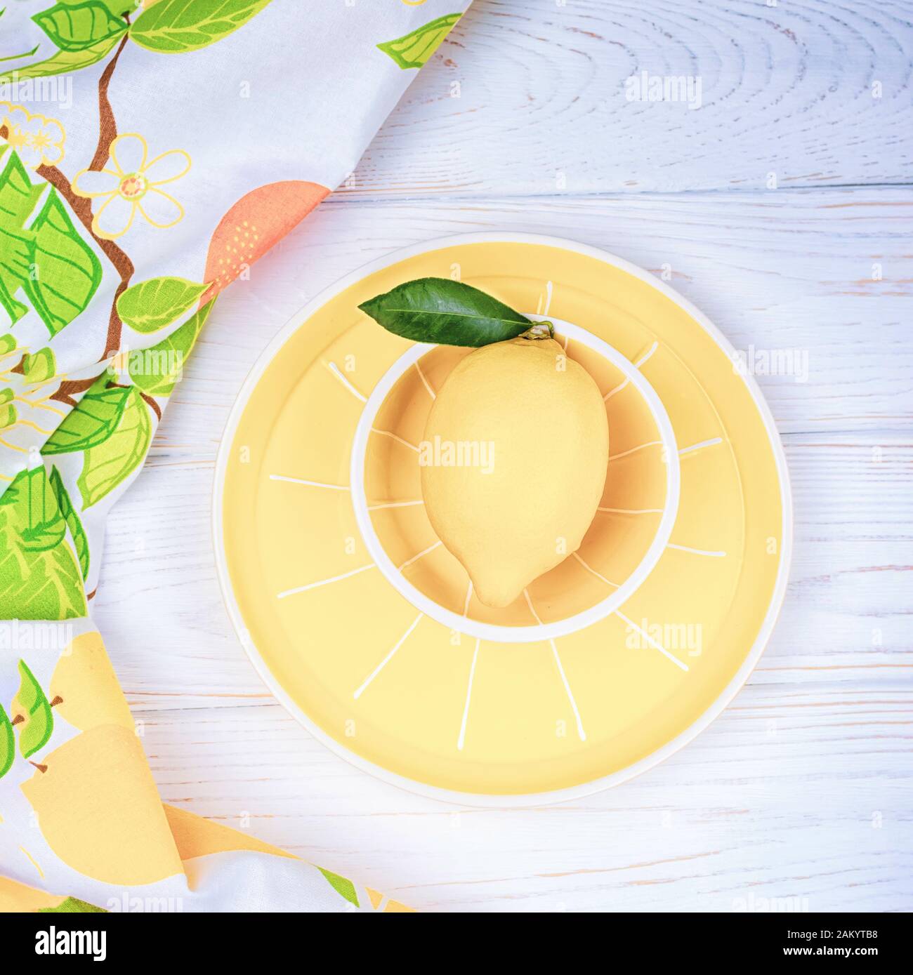 Pale pastel lemon fruit with leaf on a yellow plate. White wooden ...