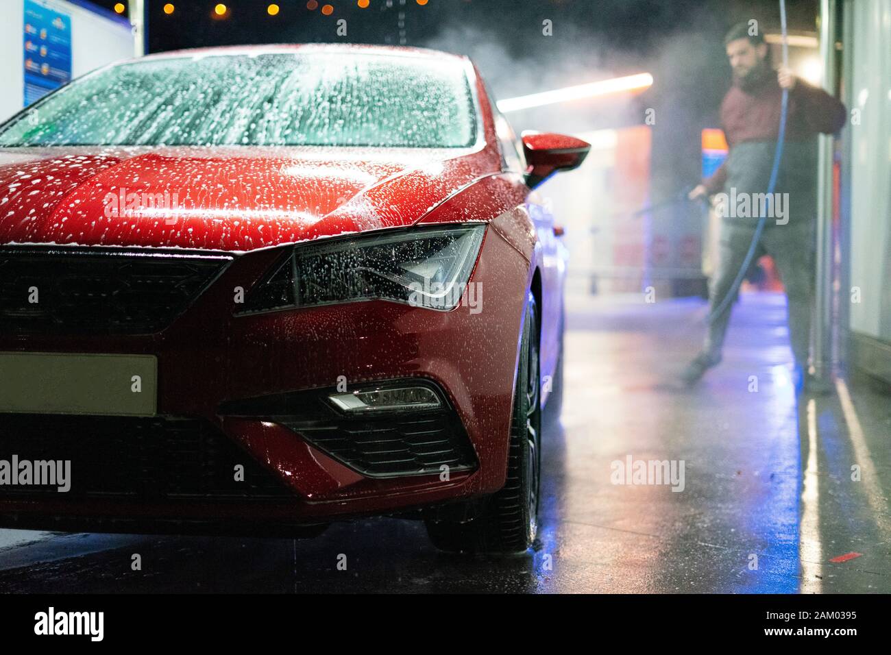Man washing a red car with high pressure water in a car wash. Car care ...