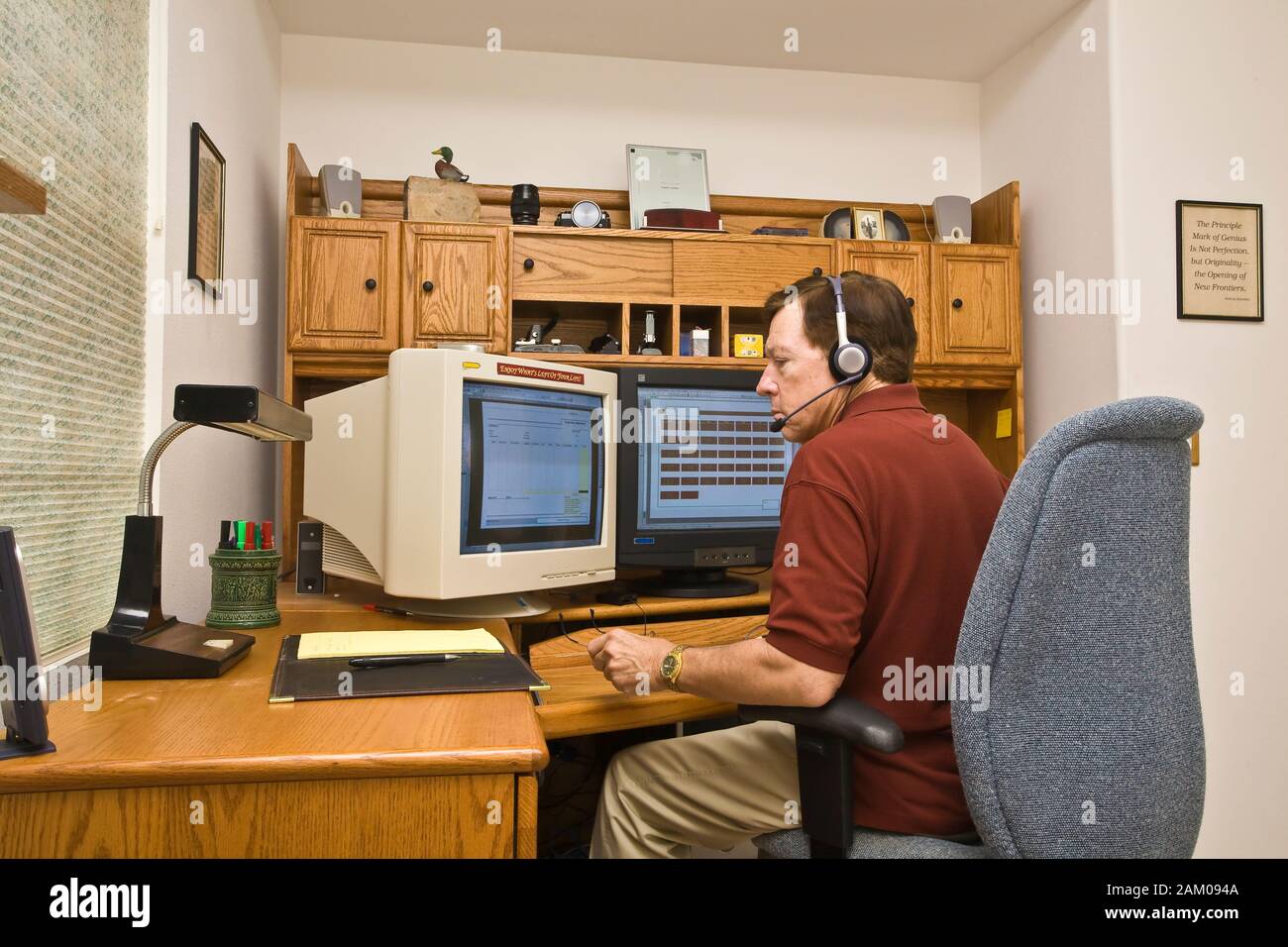 Older man sitting in office chair at computer desk with dual monitors ...