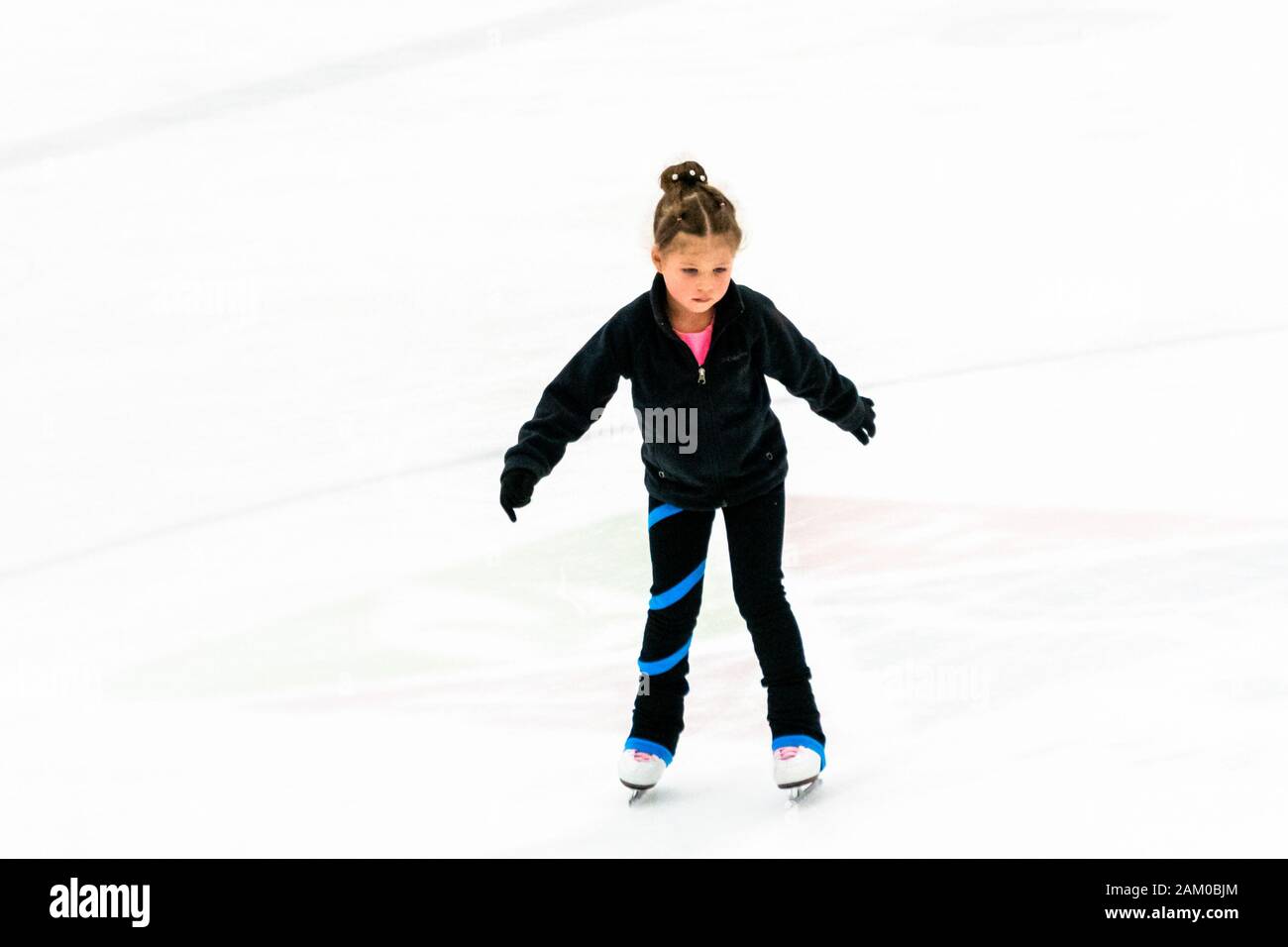 Little figure skater in black clothes practicing on the indoor ice ...