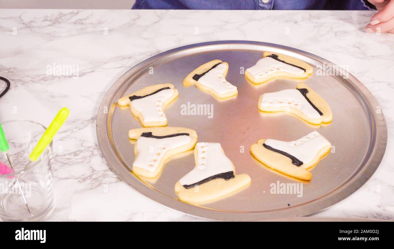 Decorating ice skate shaped sugar cookies with black color royal icing ...