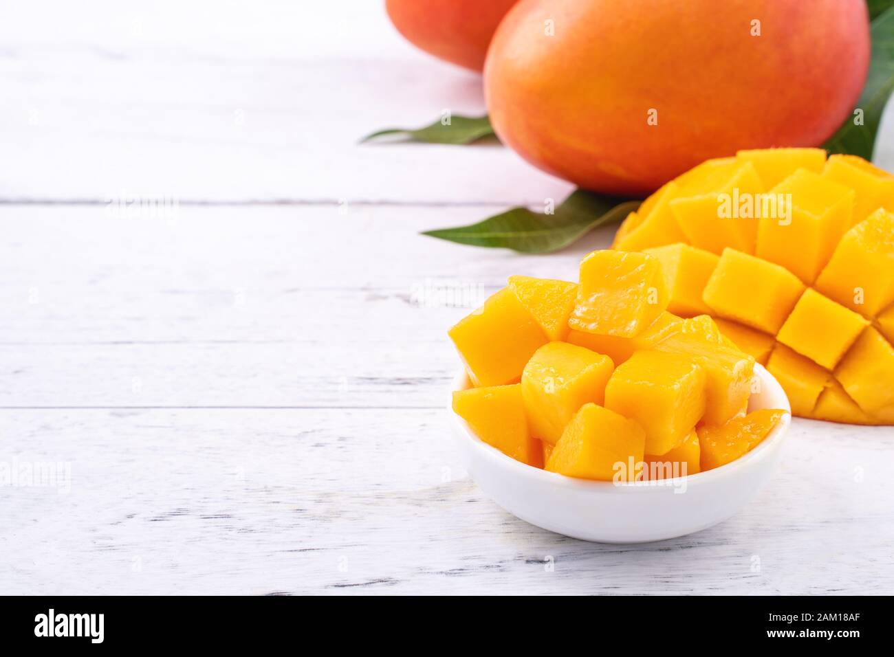 Fresh mango,beautiful chopped fruit with green leaves on bright wooden ...