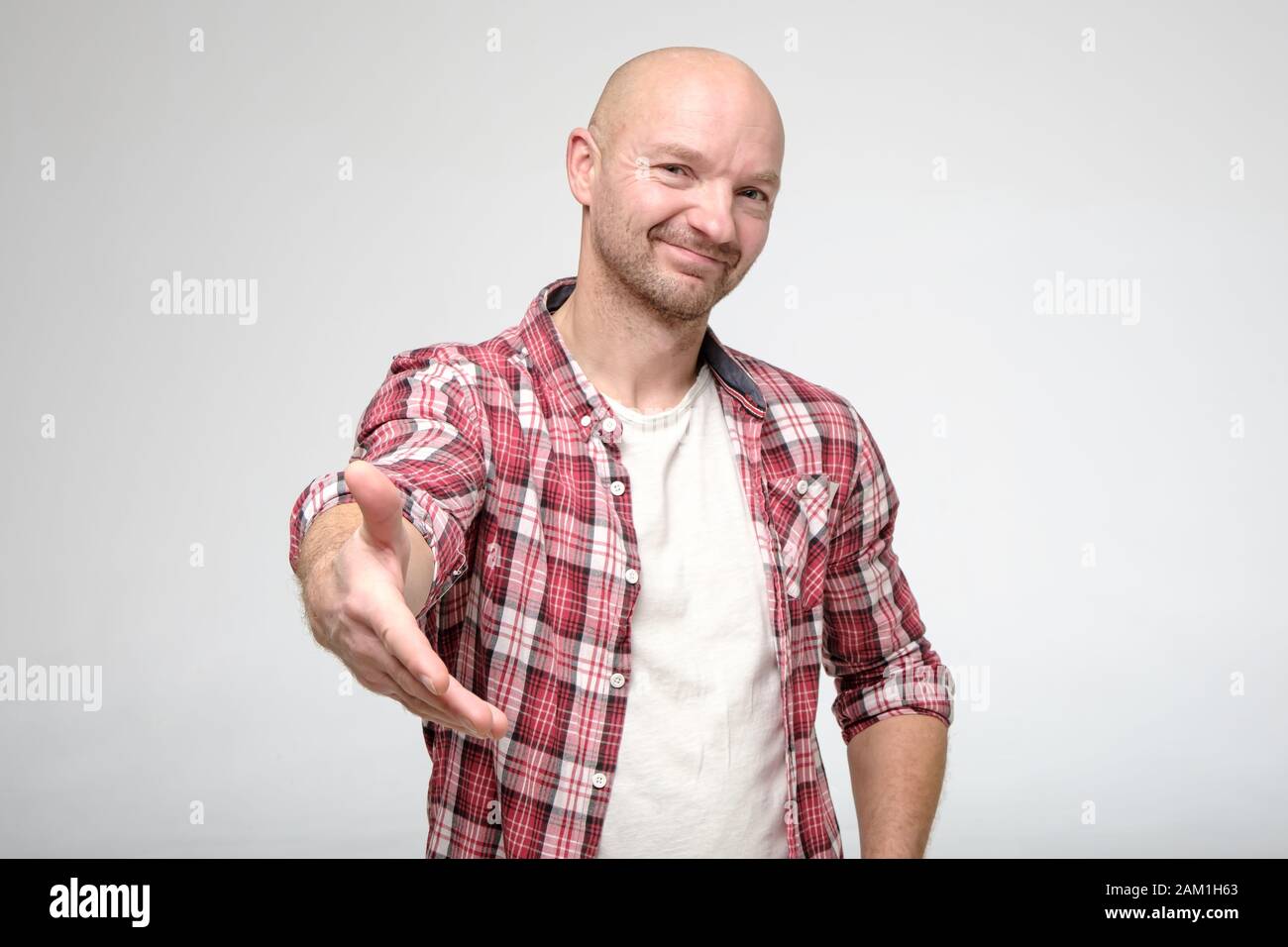 Sweet, good-natured man gives hand for handshake, looking amiably at ...