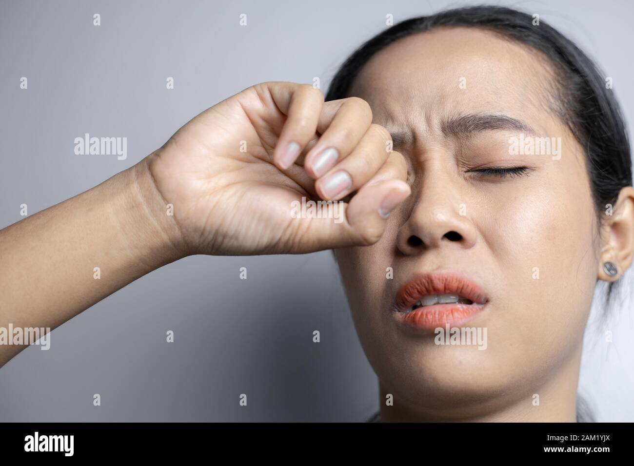 Young woman with of eye pain on a gray background. Asian woman is ...