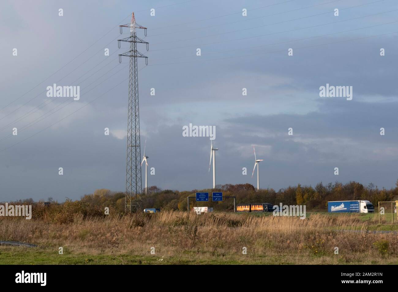 Wind turbines and electricity pylon by motorway near open pit coal mine ...