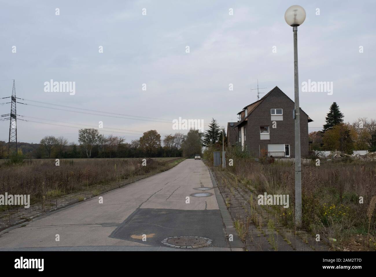 Street through flat landscape with house and electricity pylon in ...