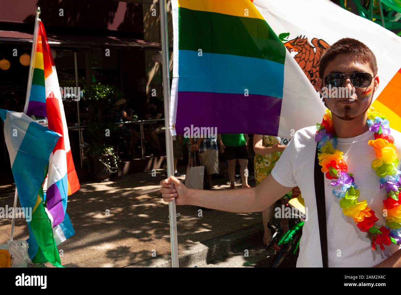 Pride parade participant wearing floral garland holding flag, crowd in ...