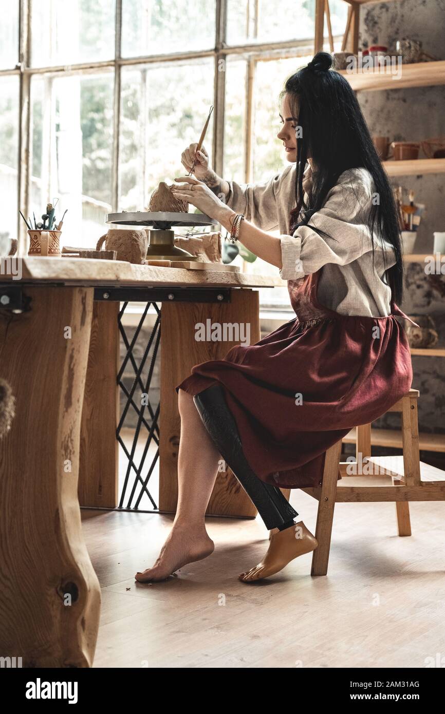 Craftsperson Concept. Young woman with leg prosthesis making pottery ...
