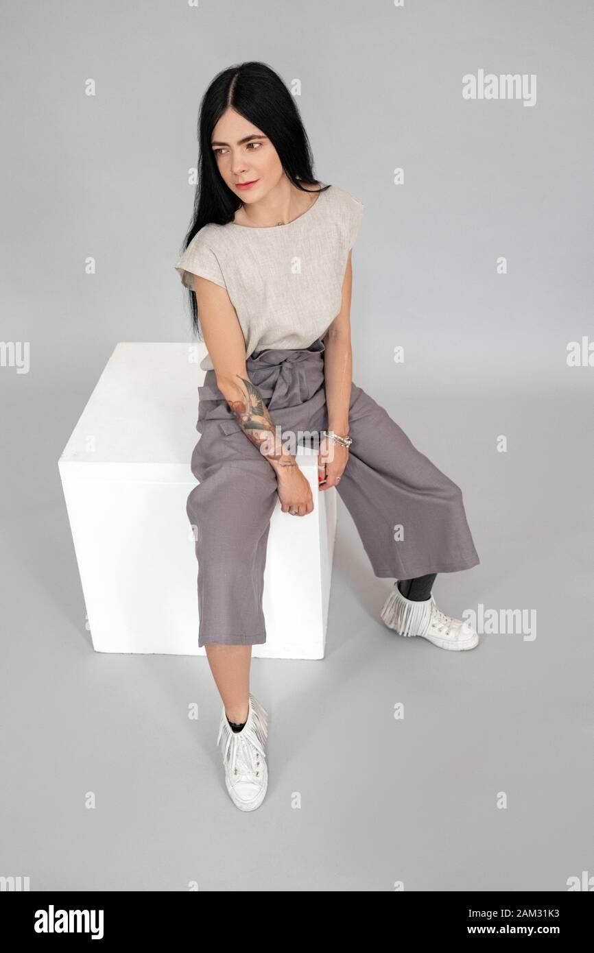 Freestyle. Diverse girl with leg prosthesis sitting on white cube ...