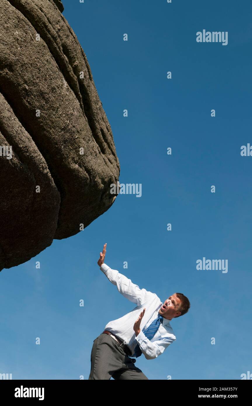 Small businessman trying to avoid massive boulder rolling down over him ...