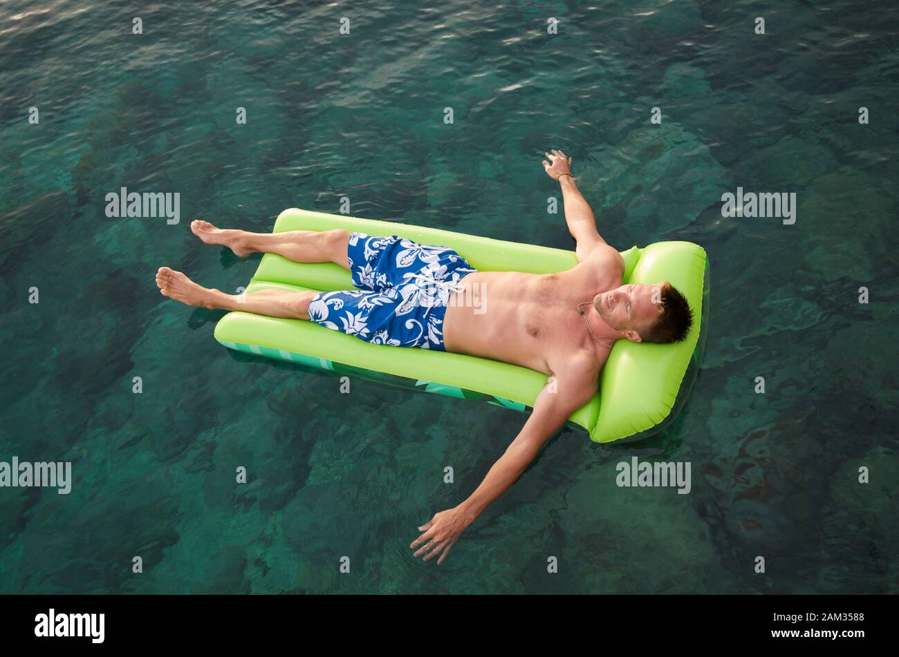 Overhead full length view of man relaxing on a green inflatable lilo ...