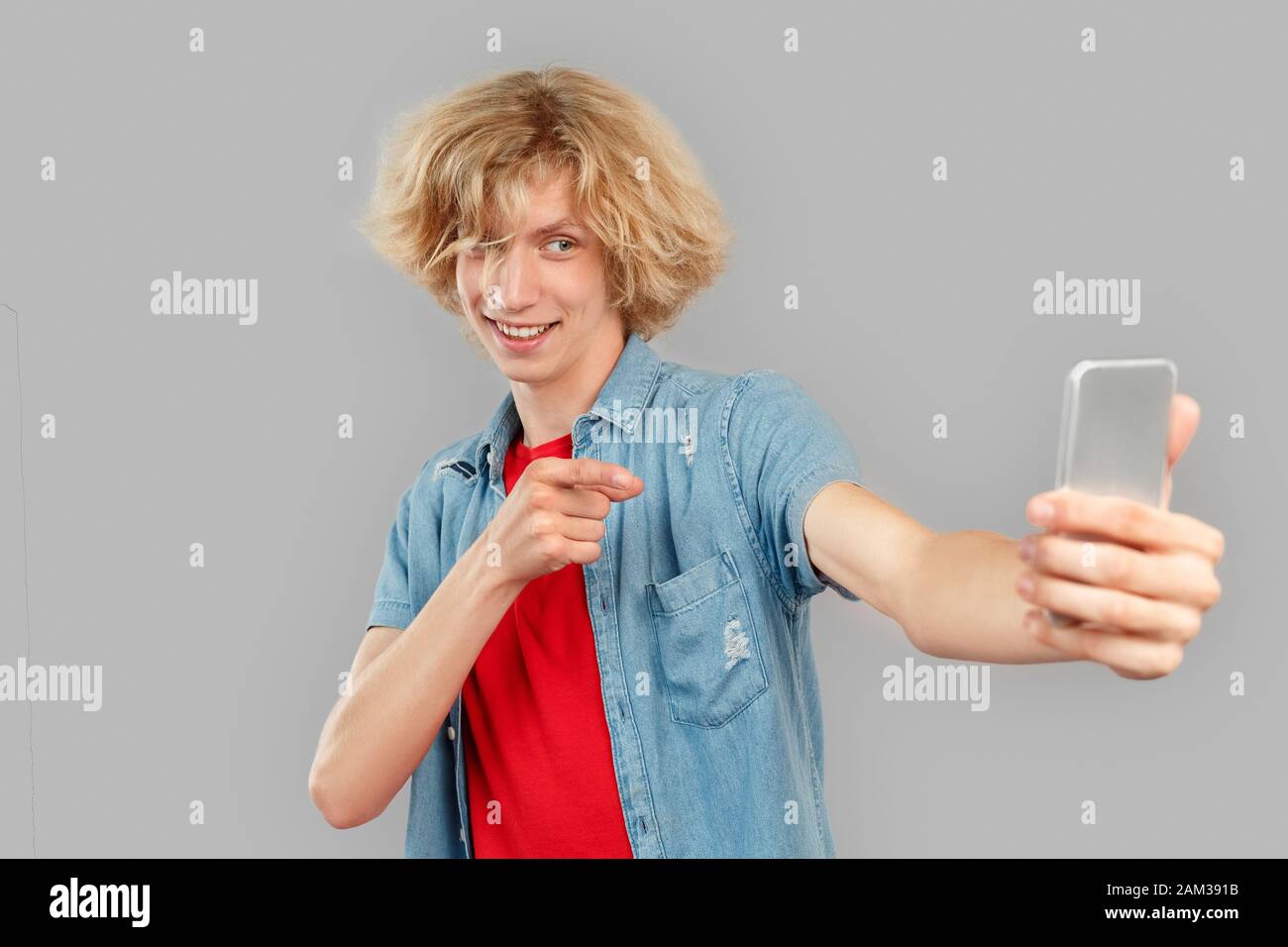 Freestyle. Teen blond boy standing isolated on gray taking selfie on ...