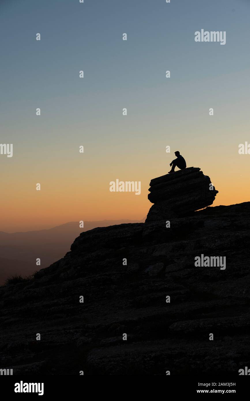silhouette of man on stones looking down while it is getting dark Stock ...