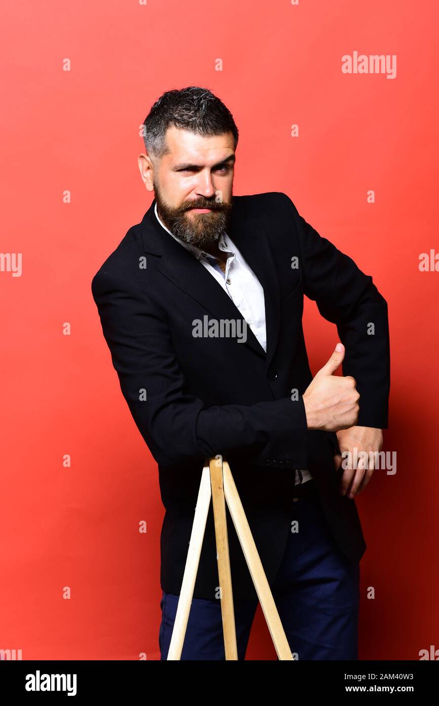 Masculinity and style concept. Macho man leans on tripod on red ...