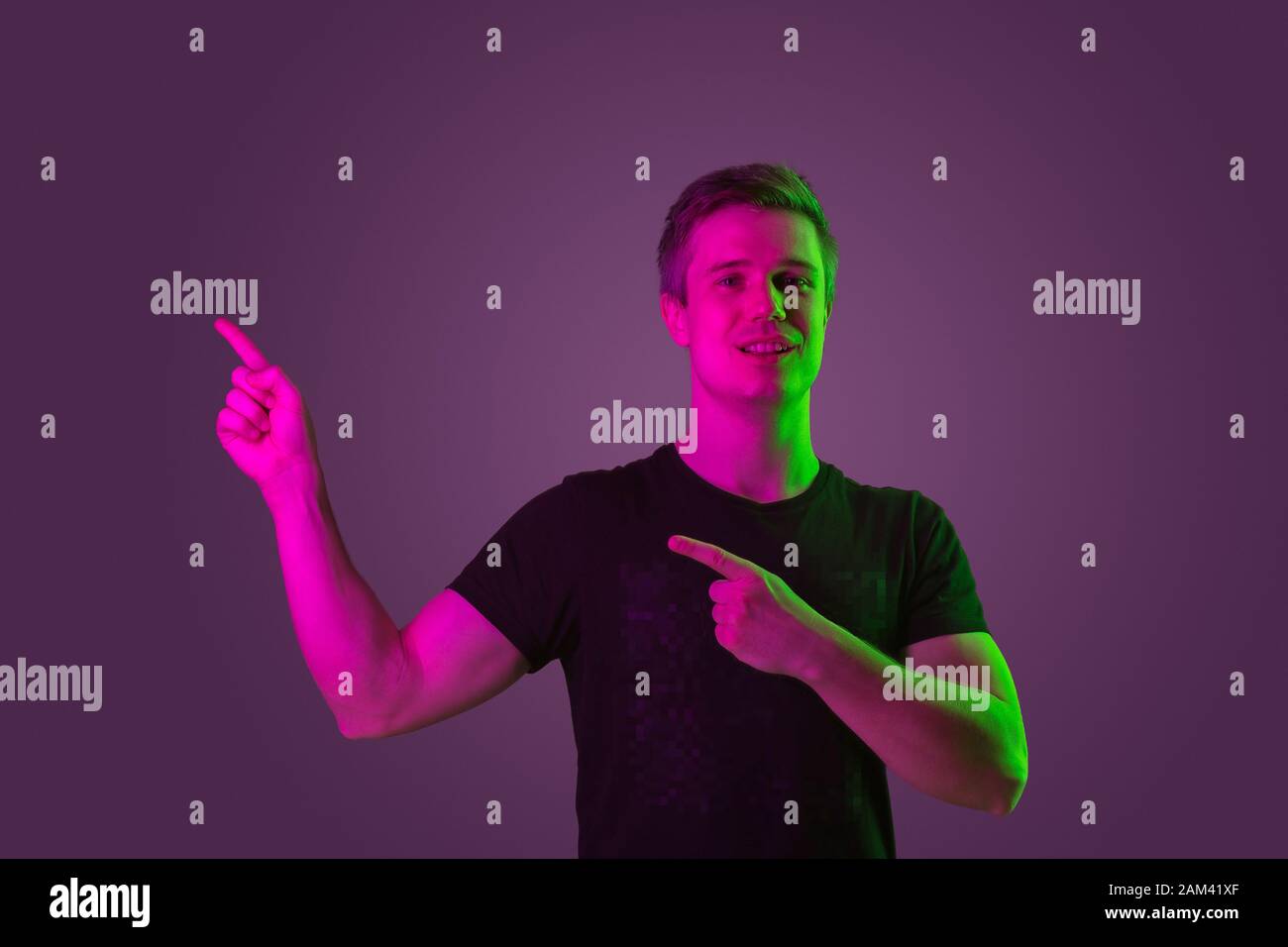 Smiling, pointing at side. Caucasian man's portrait on purple studio ...