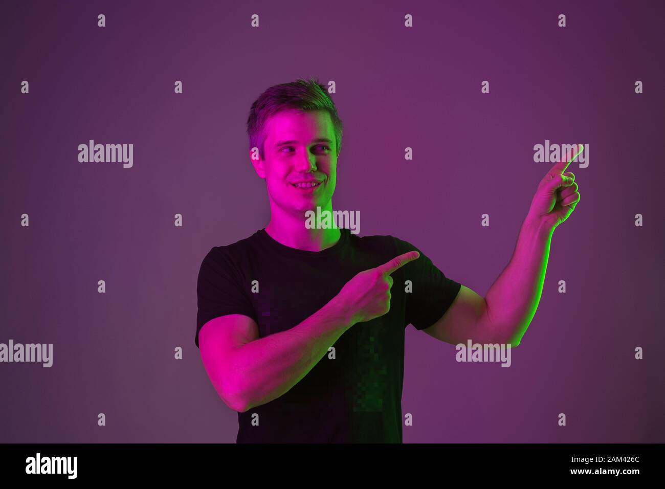 Smiling, pointing at side. Caucasian man's portrait on purple studio ...