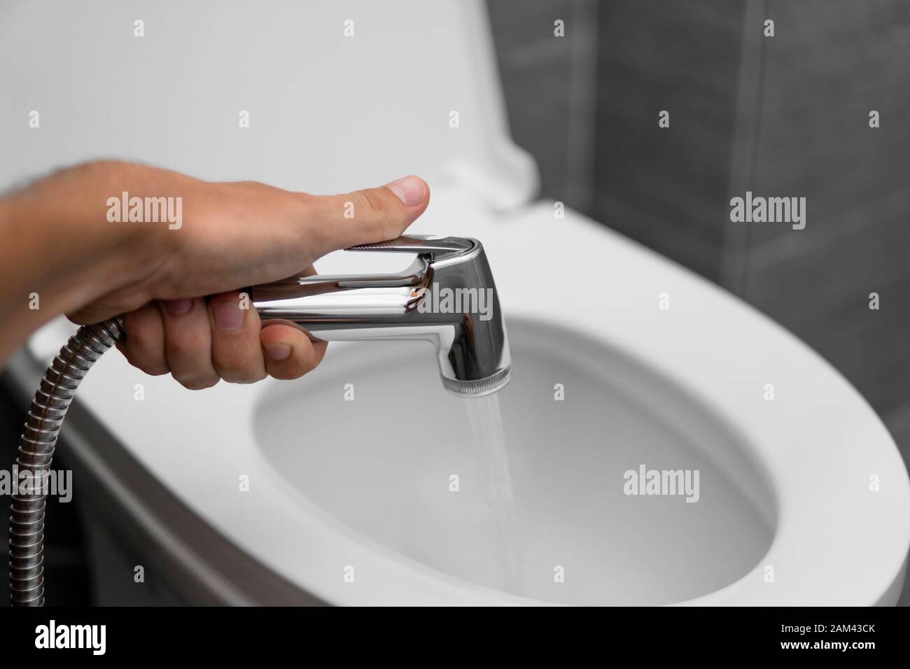Using of bidet shower with a white toilet. Bidet shower in male hand ...