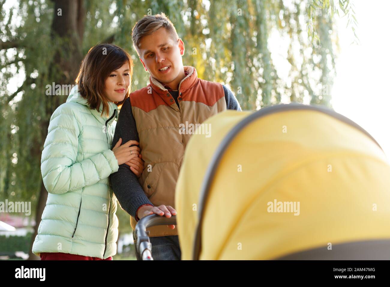 A young loving family walks by the lake with a stroller. Smiling ...