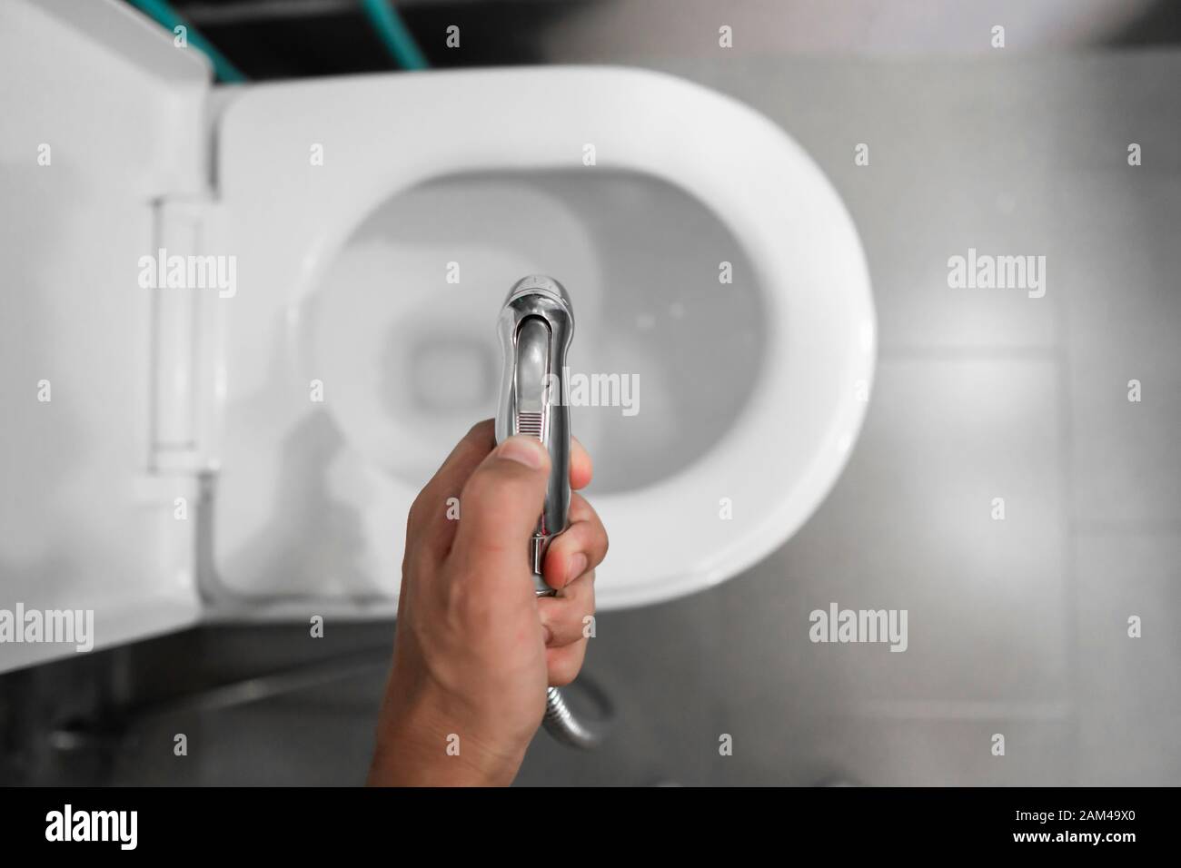 Using of bidet shower with a white toilet. Bidet shower in male hand ...