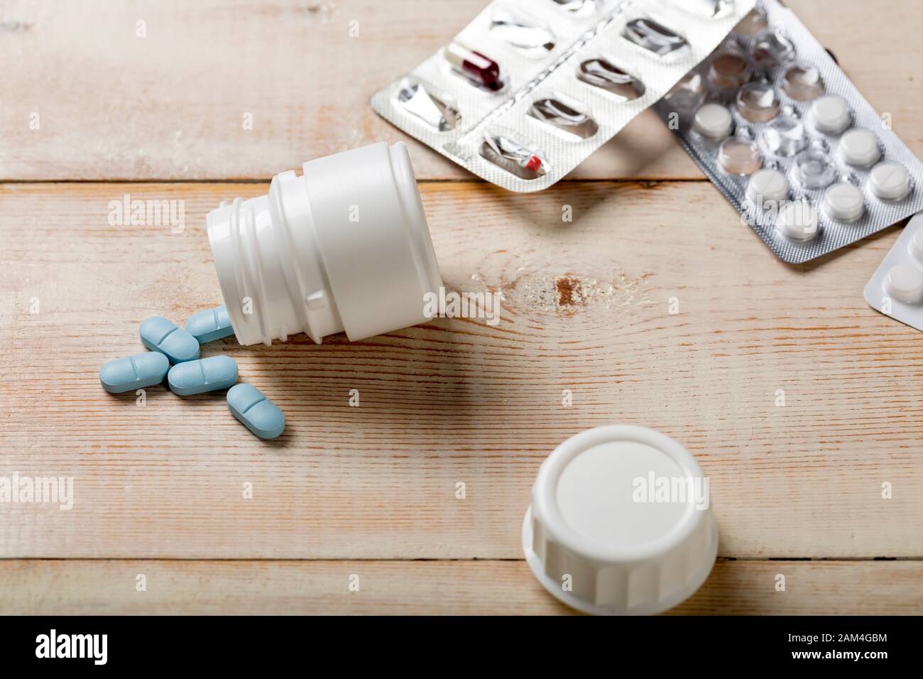 Blue pills spilled from a white plastic bottle. Different drug boxes ...
