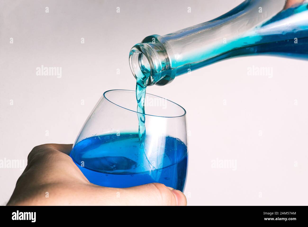 Pouring alcohol from a bottle into a glass goblet on a white background ...