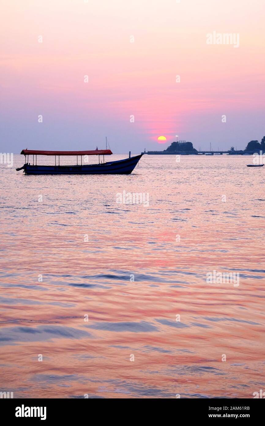 A pink glow from the sun setting over a calm sea, a Goan tourist boat ...