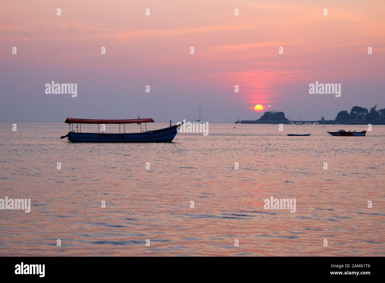 A pink glow from the sun setting over a calm sea, a Goan tourist boats ...