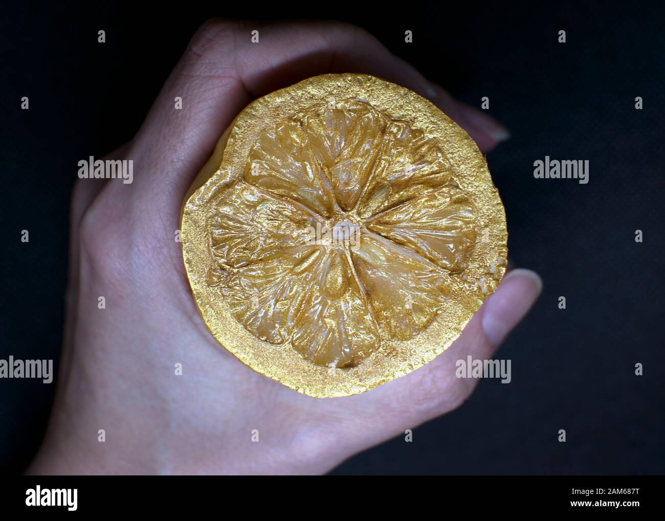 painted in gold paint cut lemon in hand. Yellow lemon in hand on a dark ...