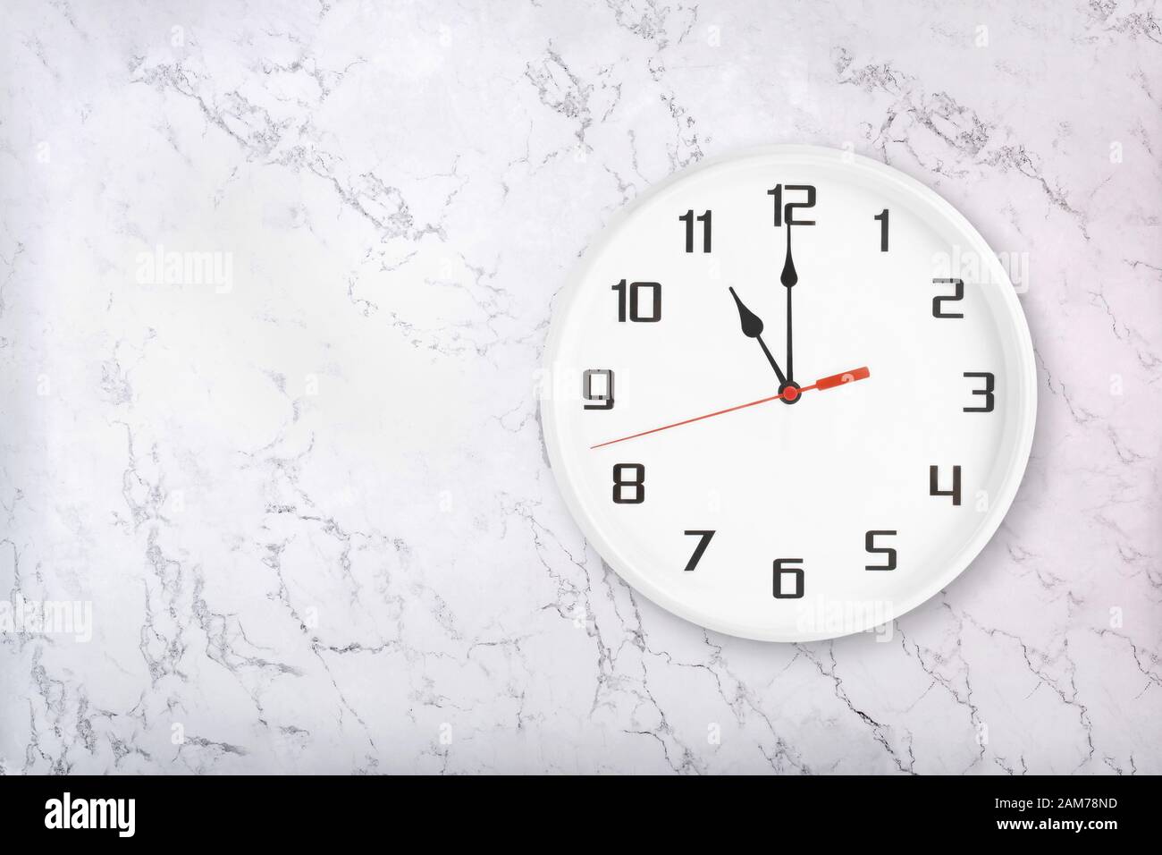 White round wall clock on white natural marble background. Eleven o ...