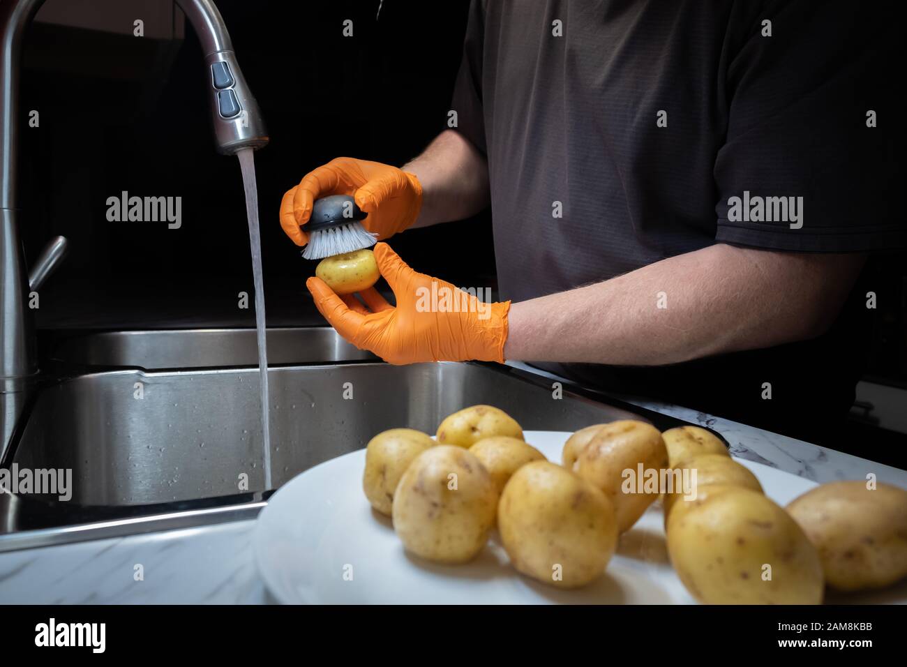 Washing and rinsing potatoes in preparation for cooking. Model wearing ...