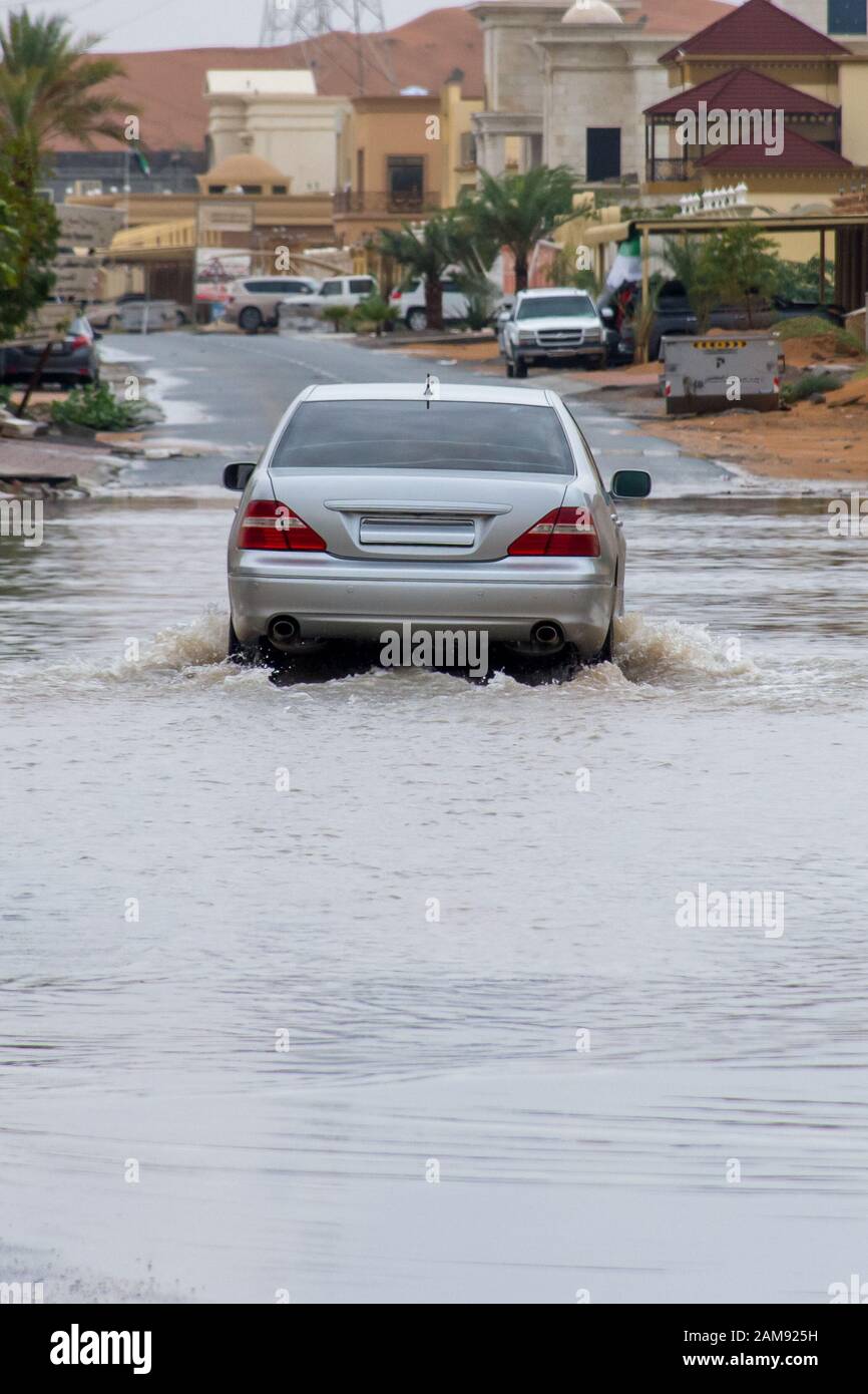 Silver Car driving through flood waters on the street making large ...