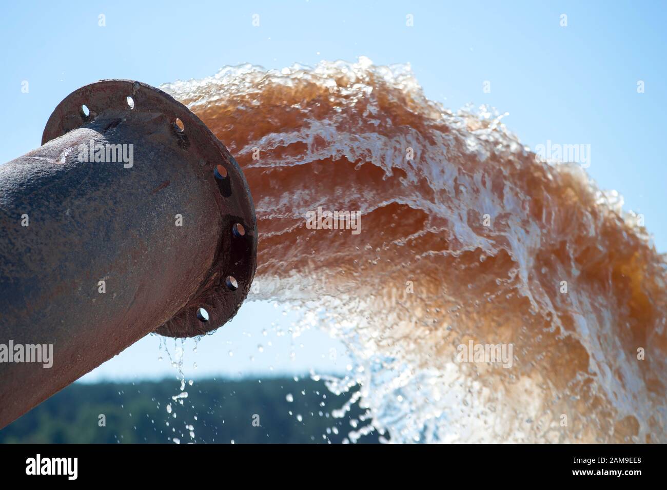 A stream of brown water bursts out of the pipe against the blue sky and ...