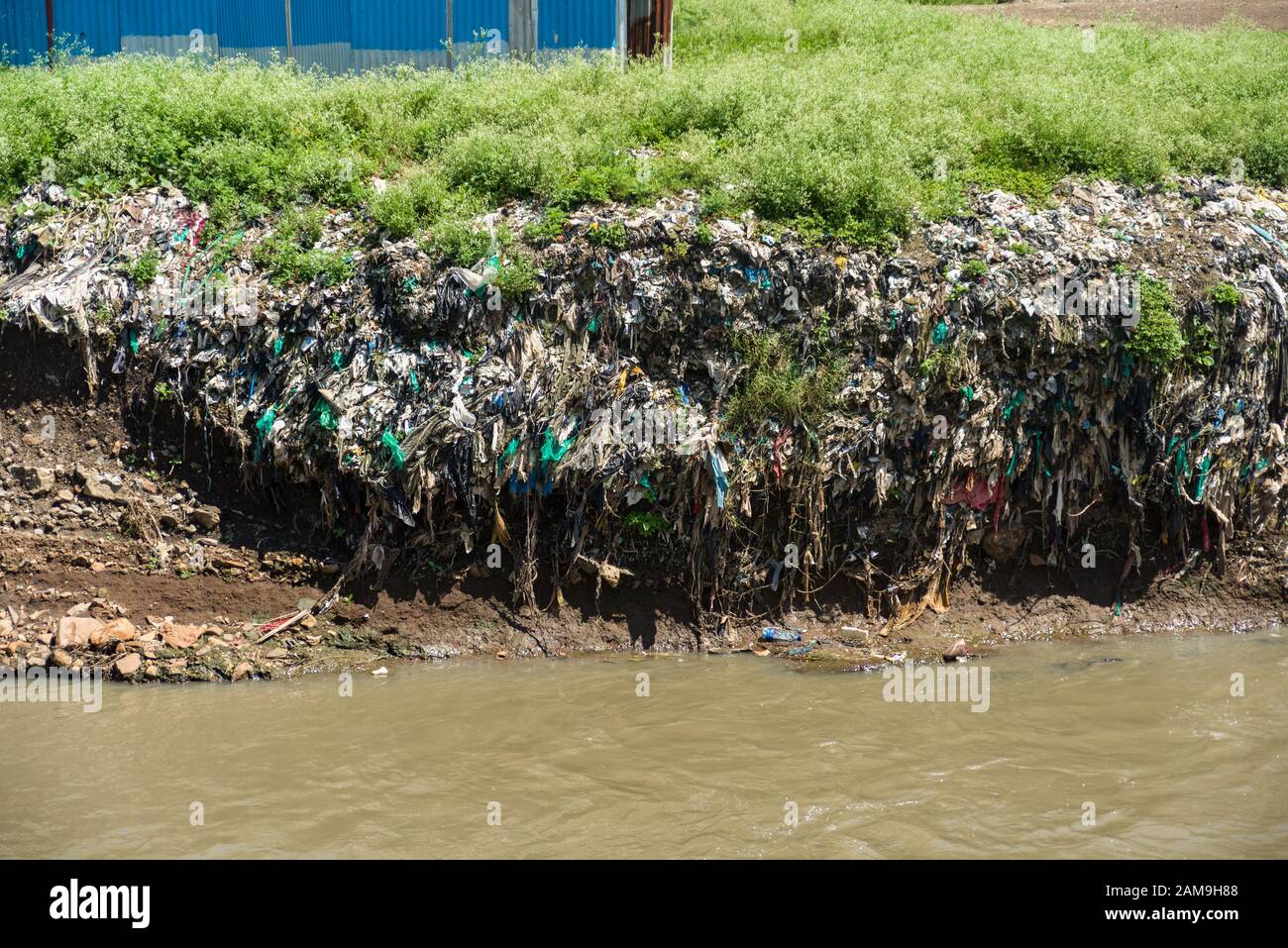 View of Nairobi river with rubbish and old clothes embedded in the soil ...