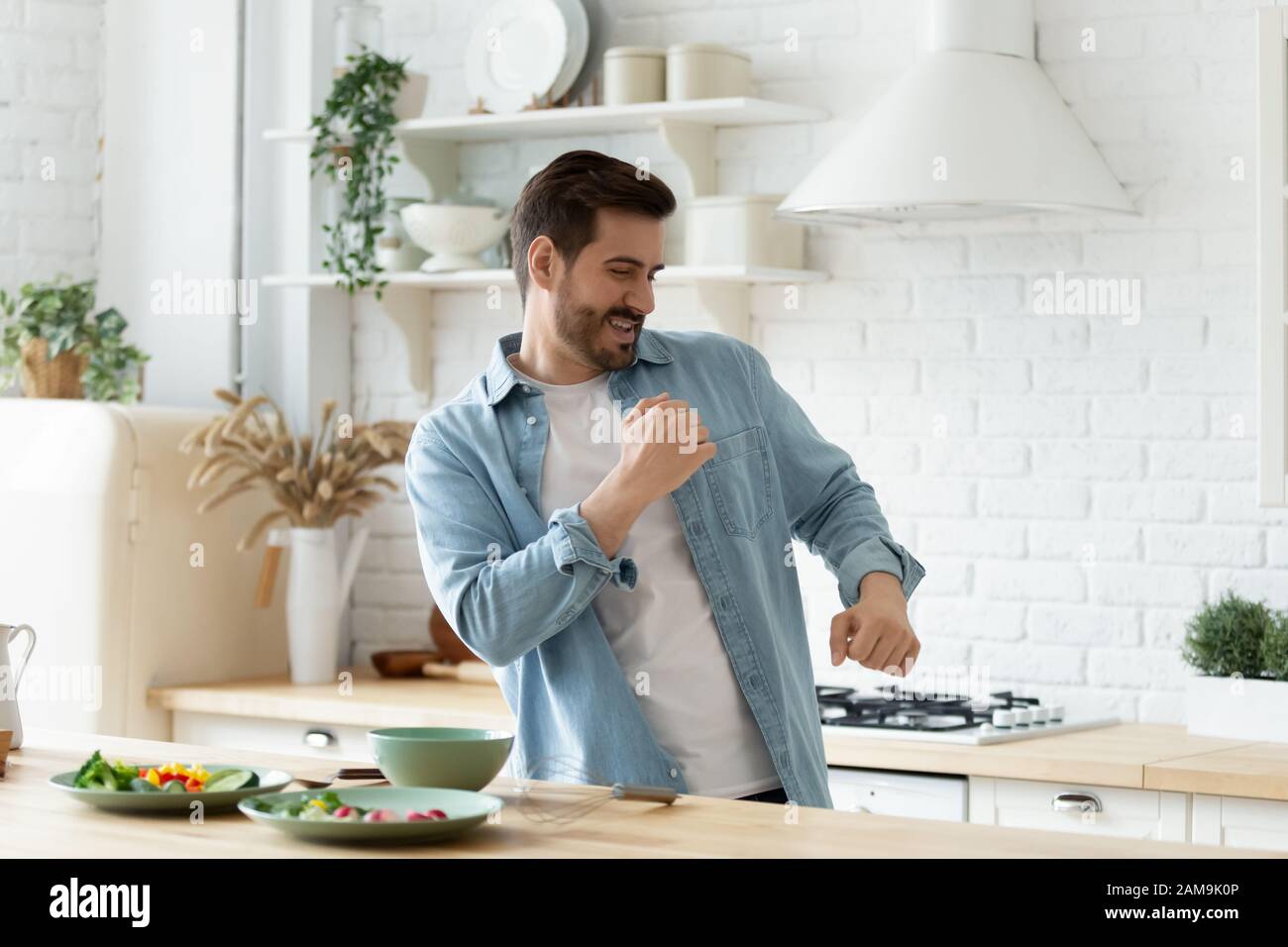 Joyful young man dancing at modern kitchen, preparing healthy food ...