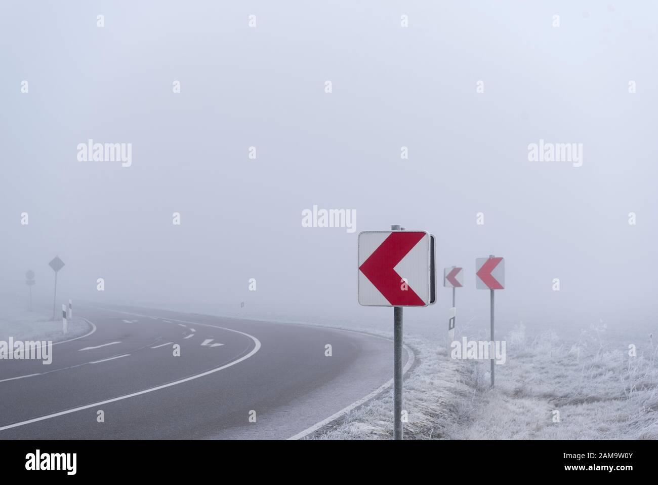 Road signs warning dangerous road curve in a dense fog. Red arrow sign ...