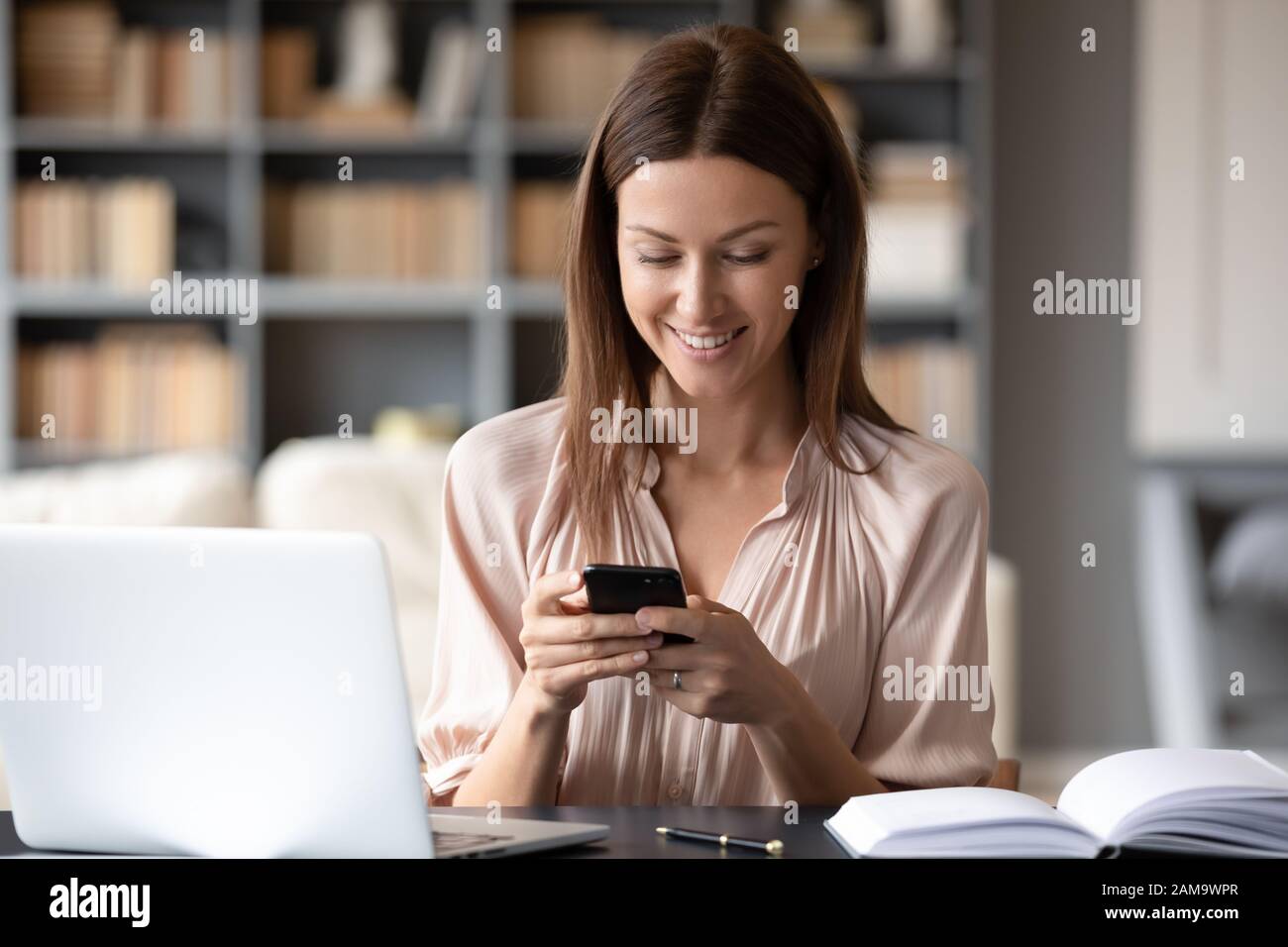 Happy young woman distracted from work using cellphone Stock Photo - Alamy